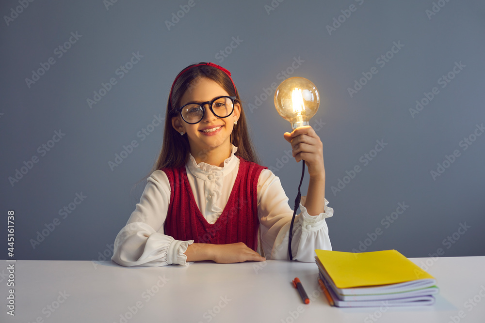 Portrait of a smart girl sitting at a school desk and holding a bright ...