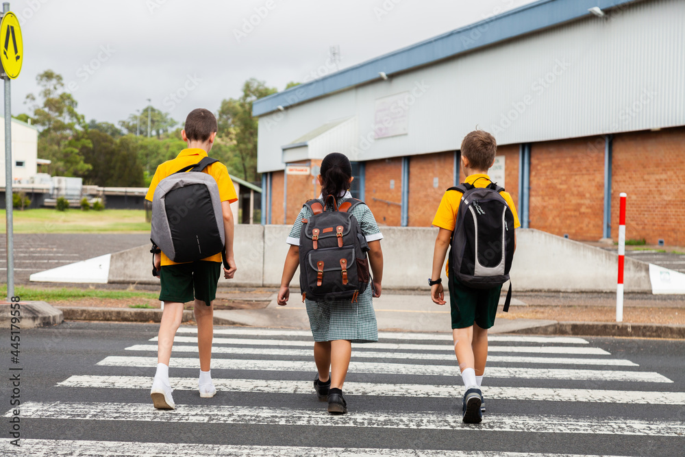 Three public school kids walking to school - crossing the road at a ...
