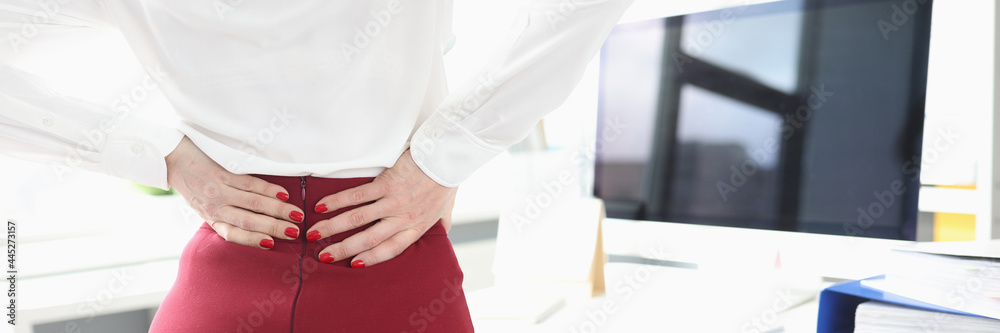 Businesswoman is standing next to her desk and feels pain in her back ...