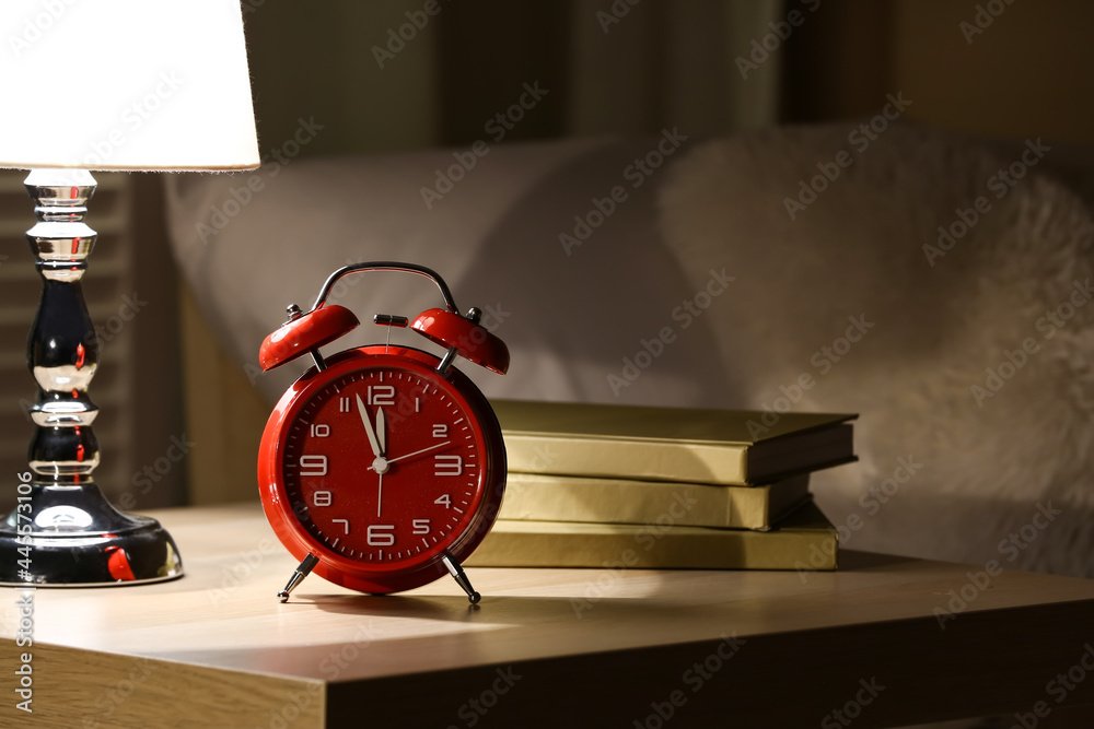 Alarm clock with lamp and books on table in bedroom at night Stock ...