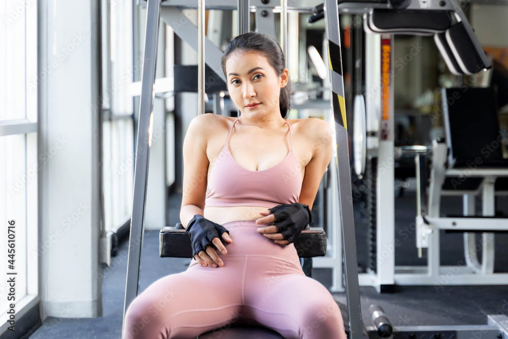 Beautiful fitness slim fit woman in sportswear sitting take a break on fitness machine in a gym ...