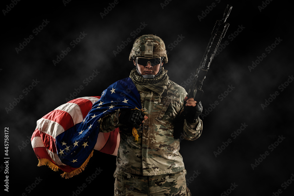 US Army soldier in combat uniforms holding the national flag across the ...