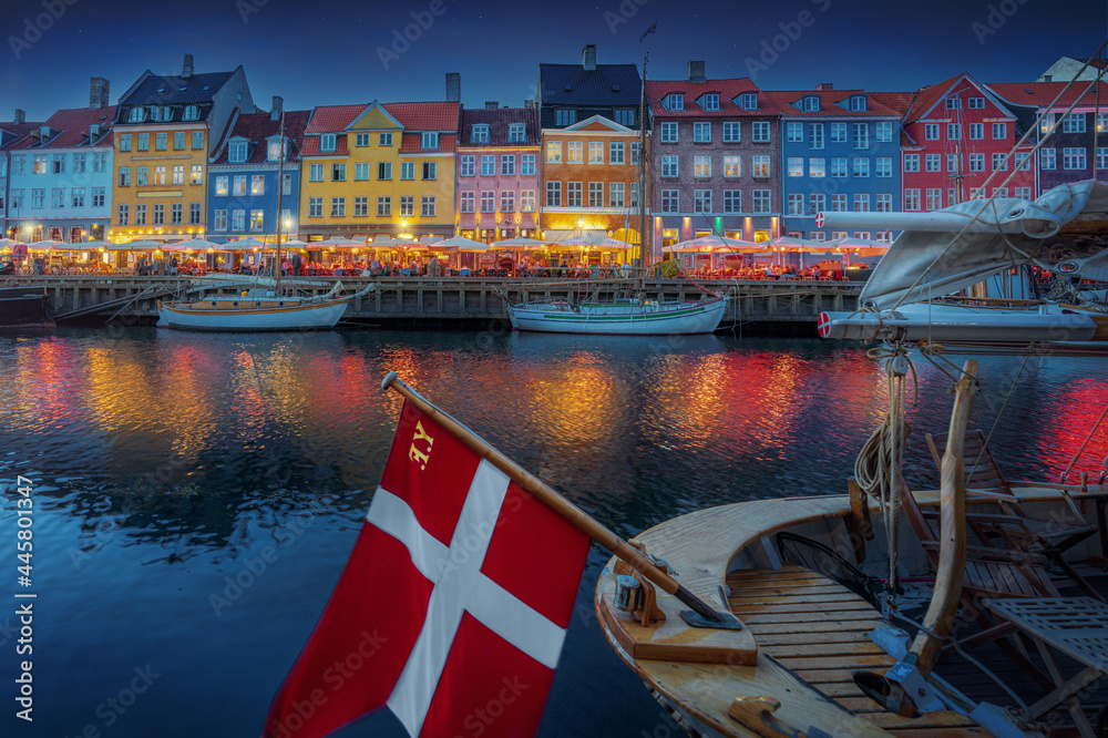 Illuminated view of Nyhavn port and waterfront at night with the flag ...