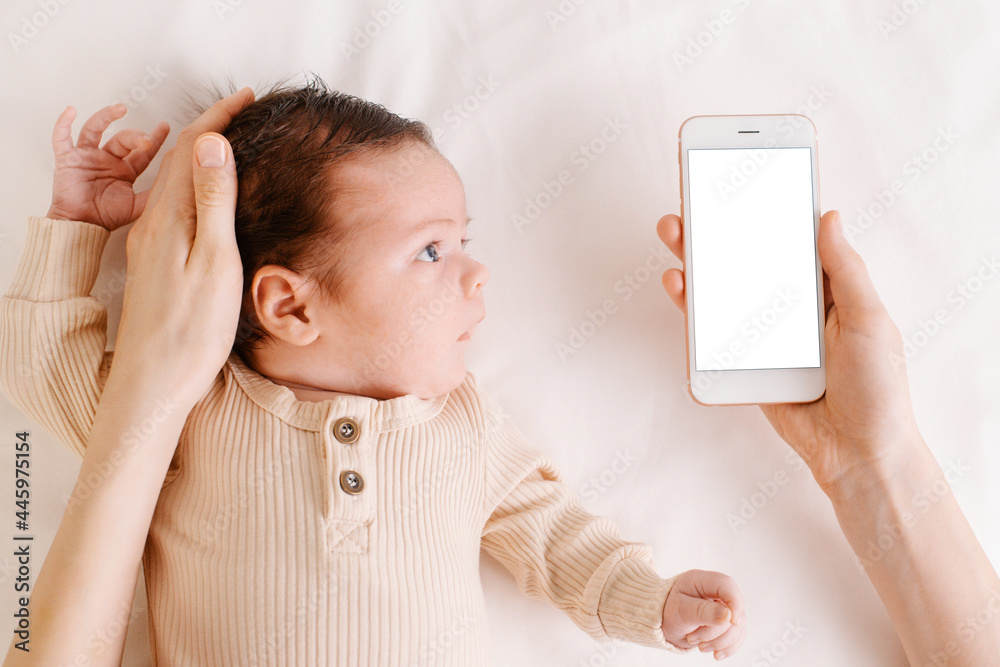 Baby newborn on white bed, woman holding mobile phone with white screen ...