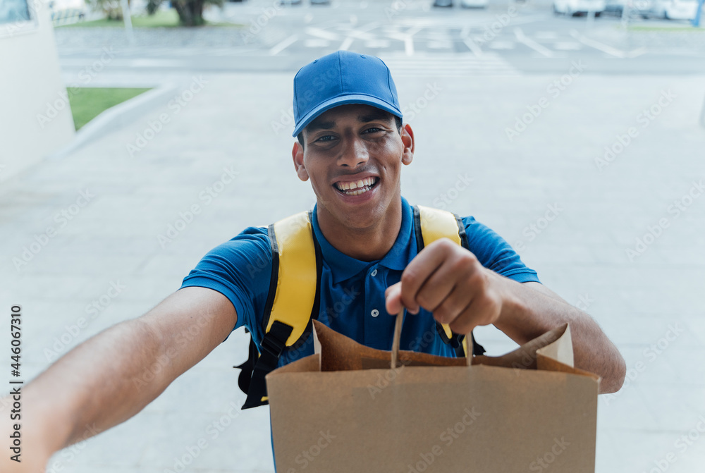 Young smiling Latino delivery man calling on intercom to deliver food ...
