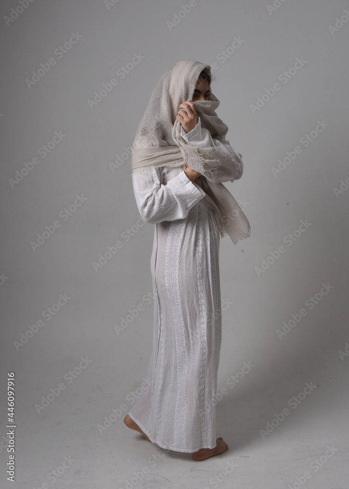 Full length portrait of young woman wearing classical white gown and a ...