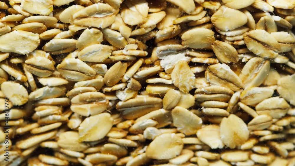 Close-up of falling down oat flakes into glass jar on blue background ...