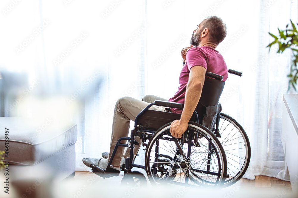 Man in Wheelchair looking out of a window at home. Rear view of mature ...