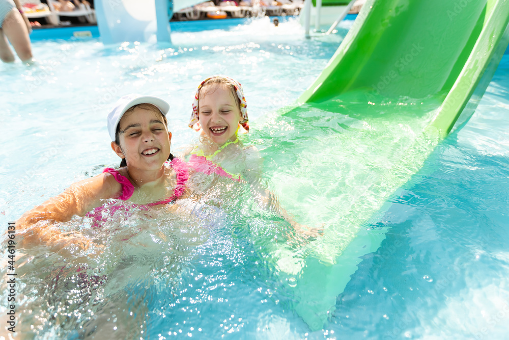 two girls splash in an outdoors swimming pool in summer. Happy children ...