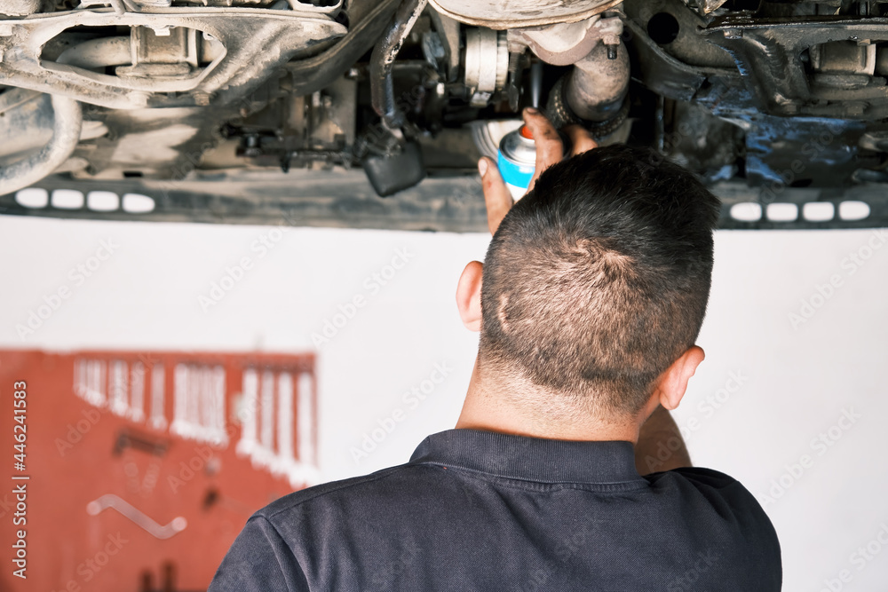 Auto mechanic using spray for the bottom parts of a lifted car at the ...