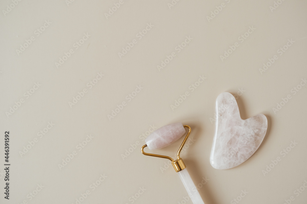 Flatlay of gua sha massage roller and stone scraper tool on neutral ...