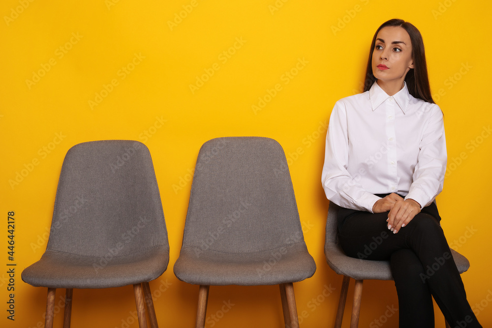 Cute stylish modern brunette woman is sitting on the chairs line on job ...