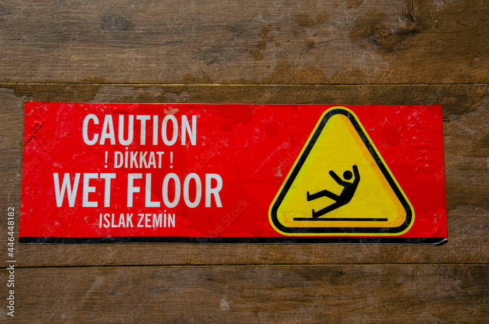 Red warning sticker for wet floor on brown tiled floor. The inscription ...