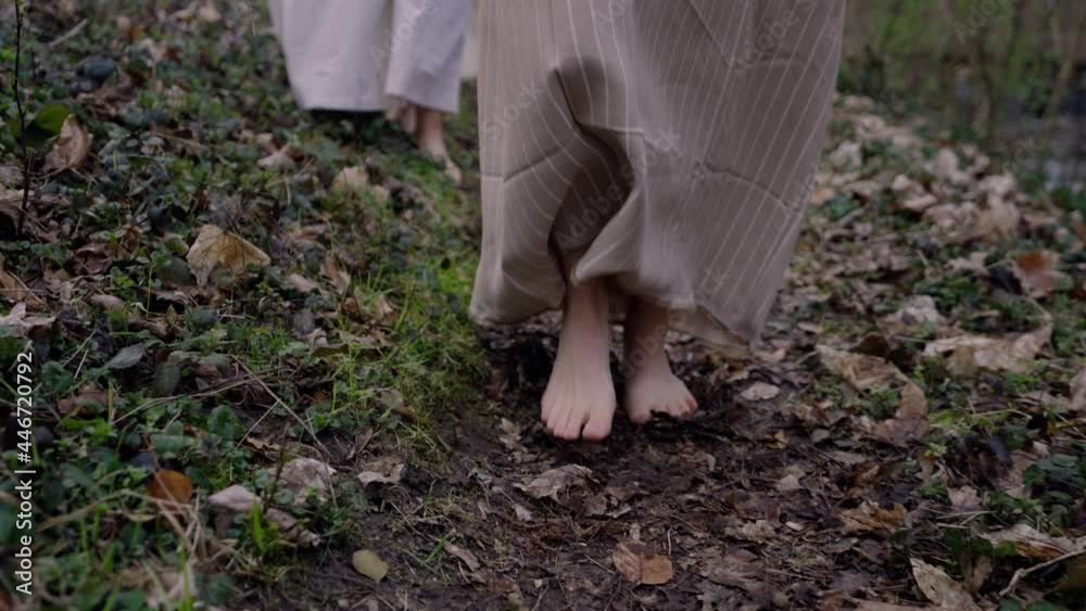 Ancient women in traditional clothing walk barefoot on a forest path ...