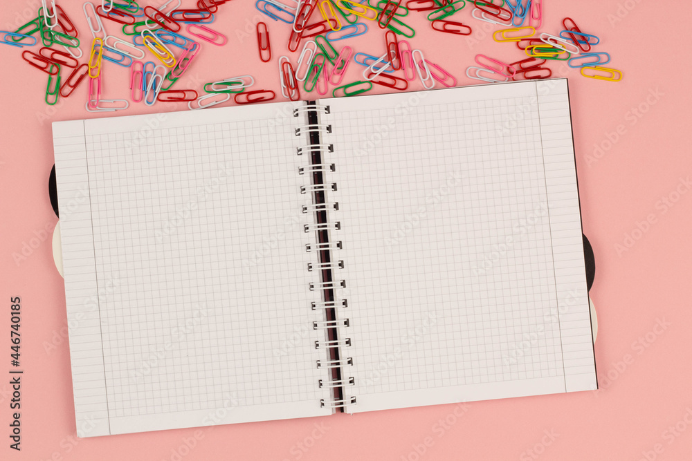 Open school squared notebook and colorful clips on the pink background ...