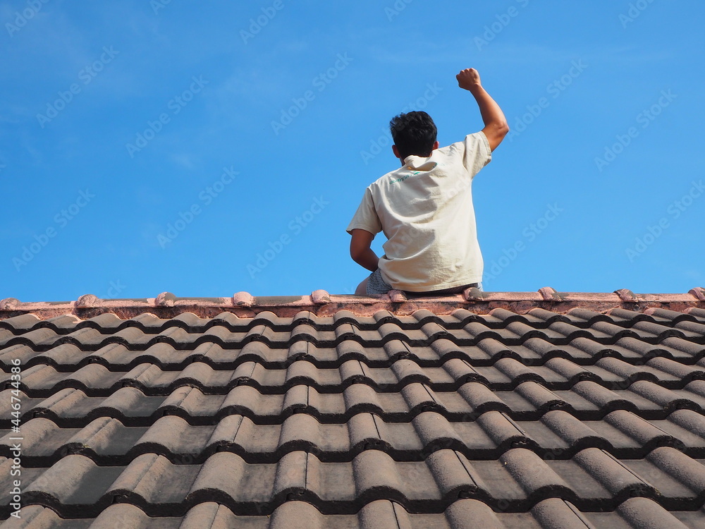 Man sitting on black roof and show hand up with blue sky background and ...