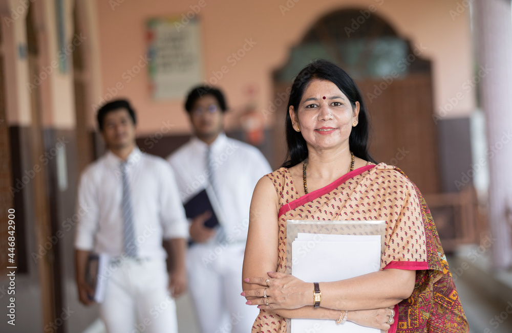 Confident smiling Indian school teacher with students in background ...