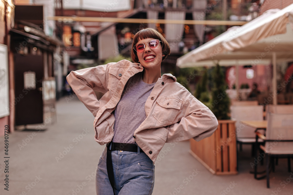 Good-humored girl with short hair in denim jacket and pink sunglasses ...
