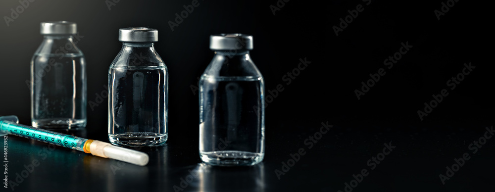 Three clear vaccine bottles with no labels on black background green ...