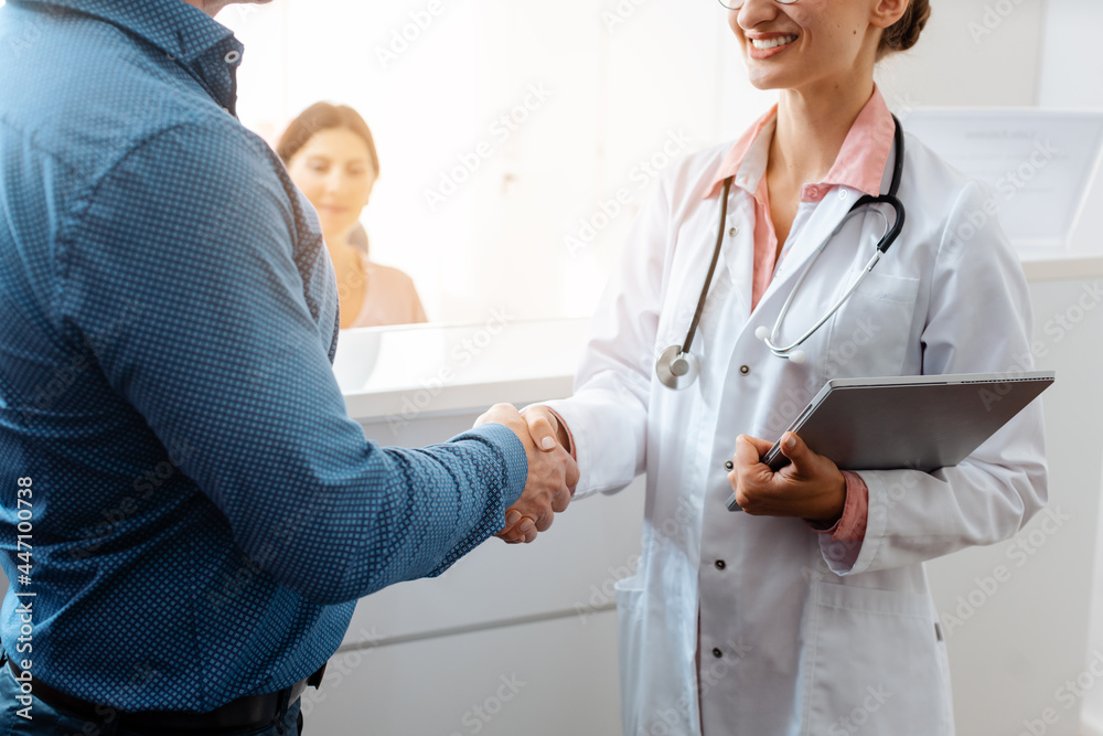 Doctor and patient greeting each other and shaking hands at front desk ...