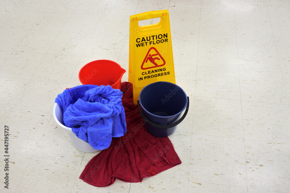 Caution slippery floor sign beside buckets and towels on a wet floor ...