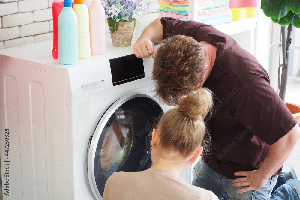 Caucasian couple looking at their washing machine broken at home while ...