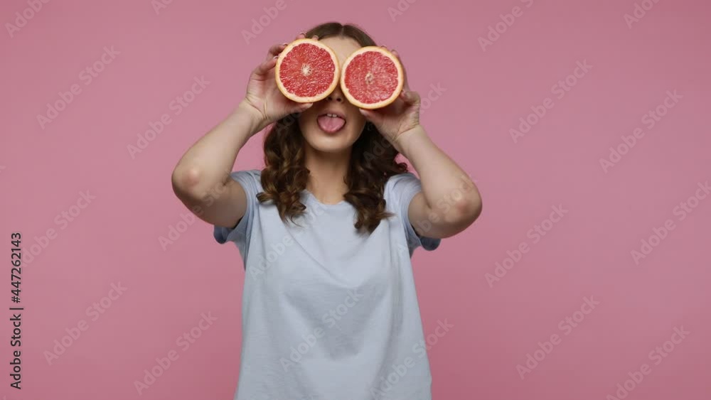 Happy optimistic teenager girl covering eyes with halves of grapefruits ...