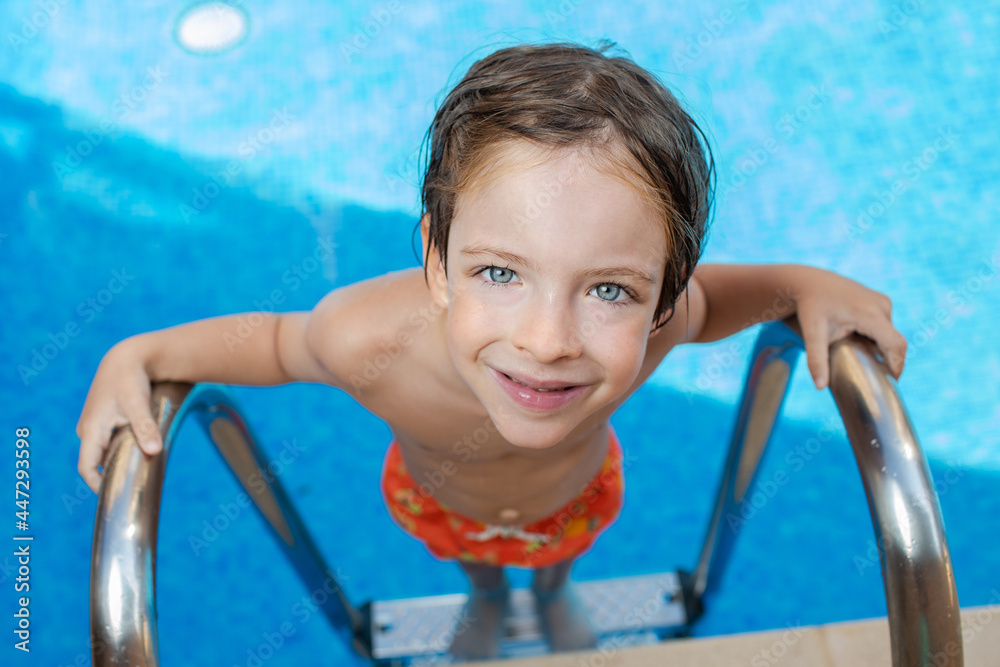 A beautiful and cute little boy with wet hair gets out of the pool. A ...