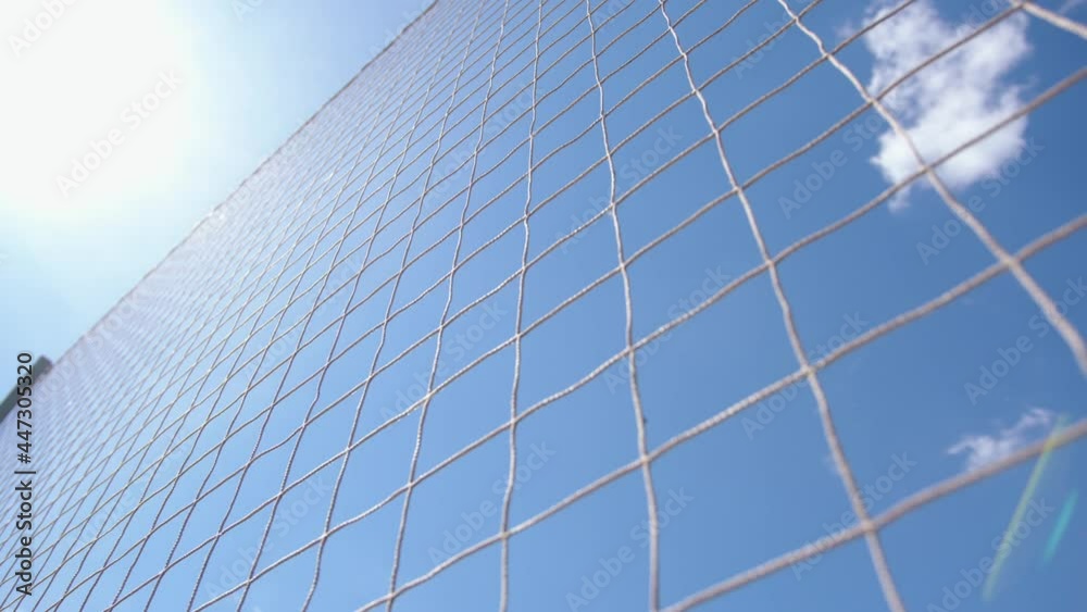 Blue sky with white clouds and a bright sun through a fencing made of ...