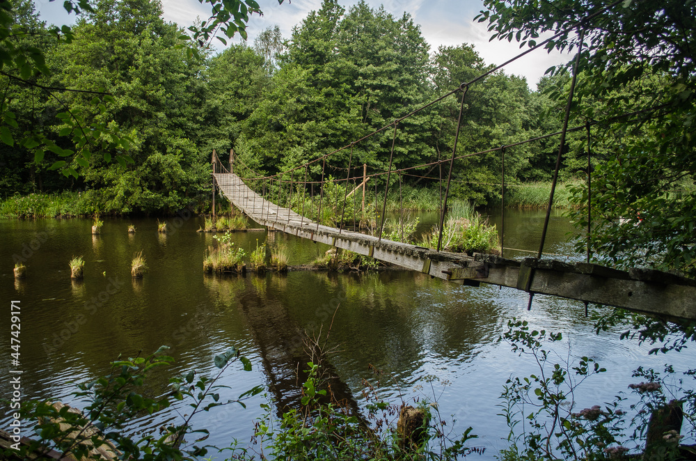 Old and damaged rope and wooden boards bridge over the river Irbe ...
