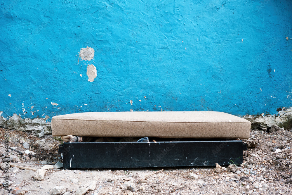 Old discarded mattress and bed in front of a blue wall. Homelessness or ...