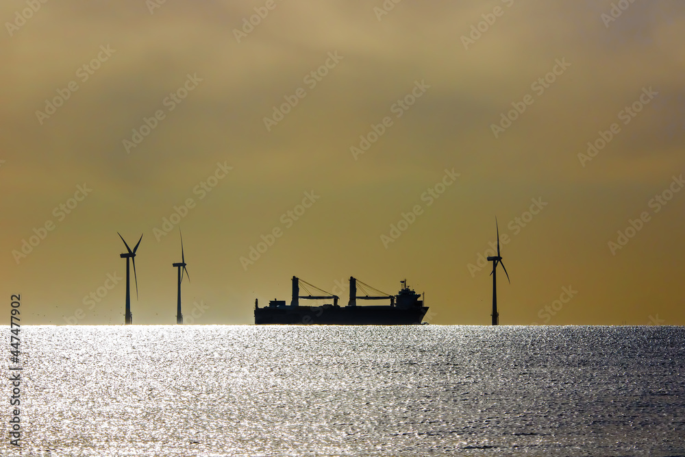 Clean energy. Heavy transport ship sihouetted between offshore wind ...
