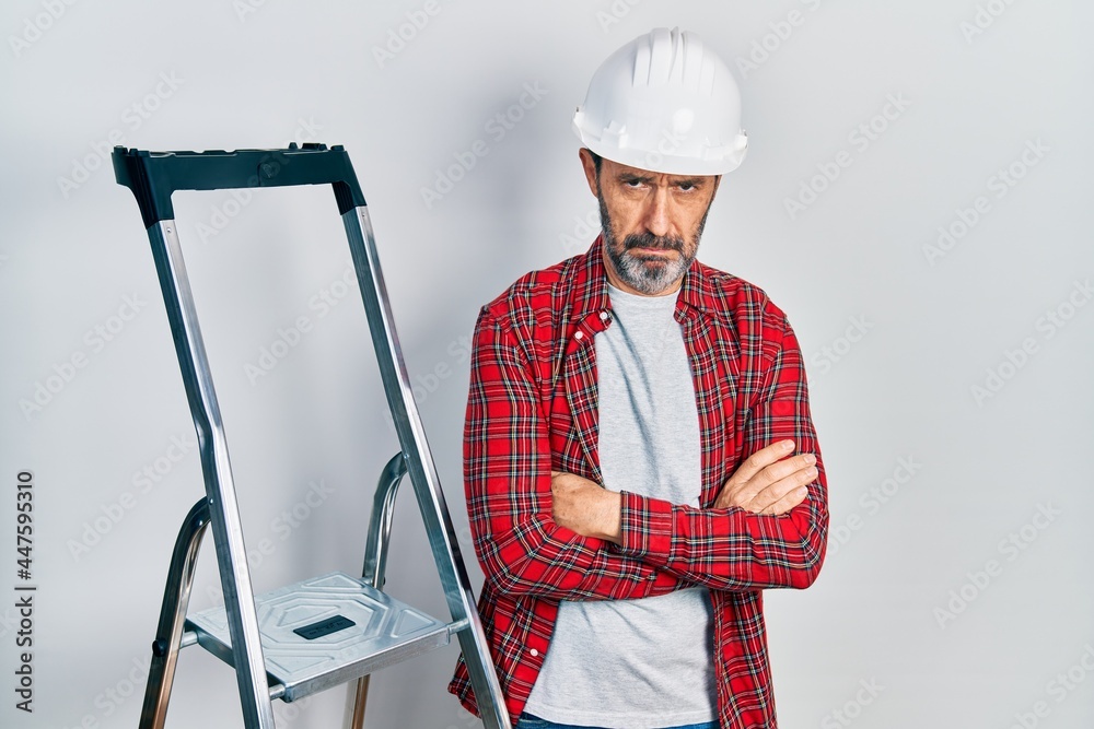Middle age hispanic worker man with arms crossed gesture using ladder ...