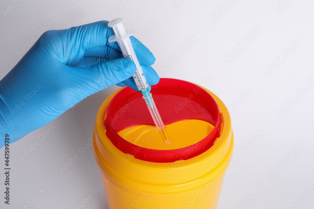 Doctor throwing used syringe into sharps container on white background ...