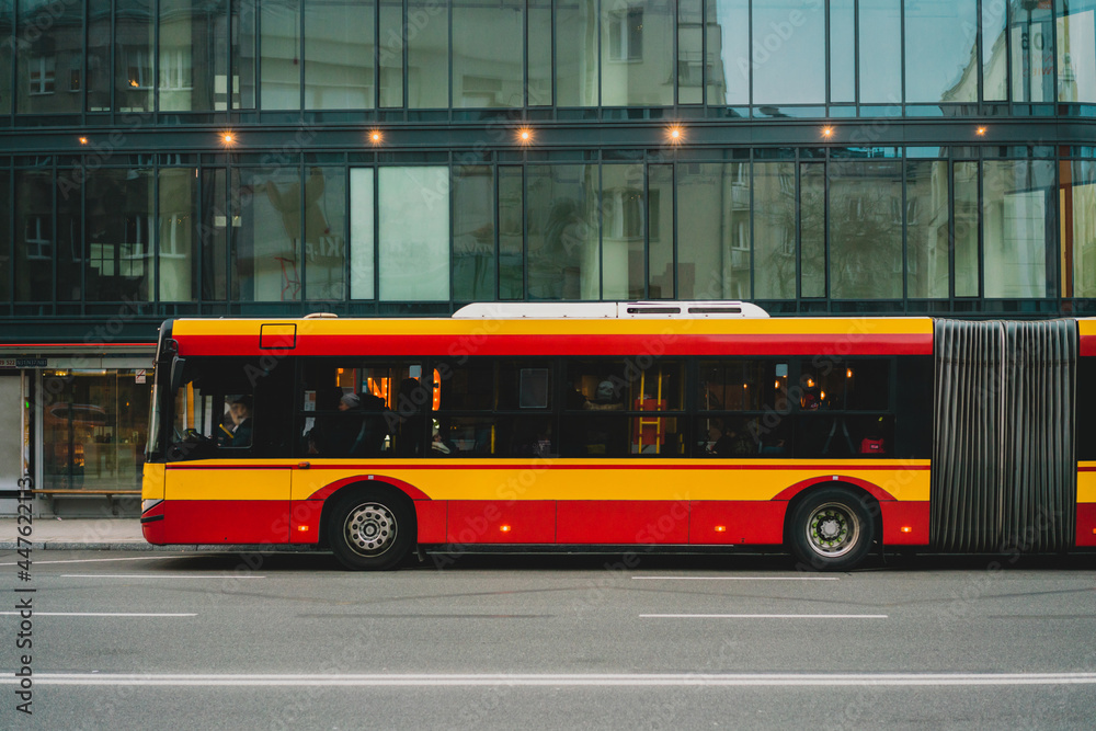 A yellow and red articulated bus parked near business center in the ...