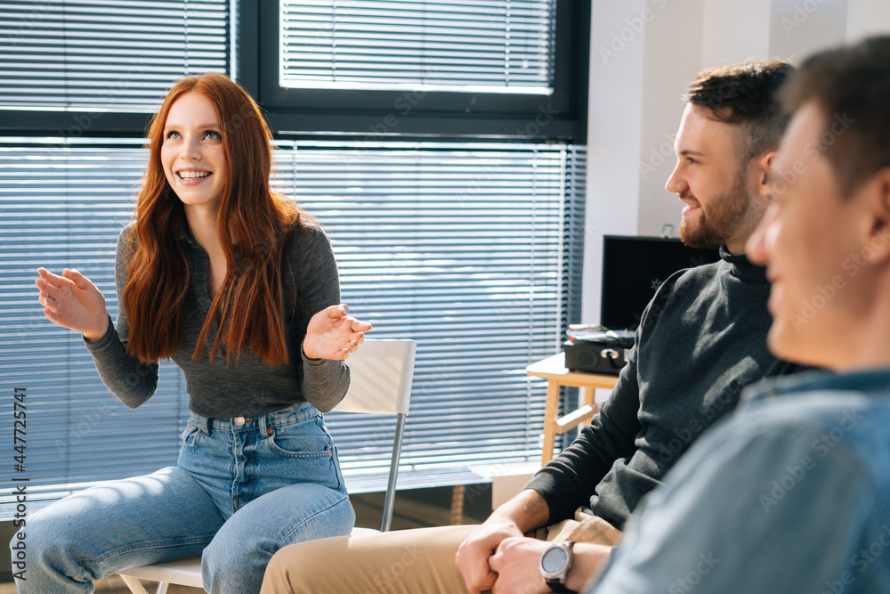 Happy redhead young woman talking new ideas with creative team, during ...
