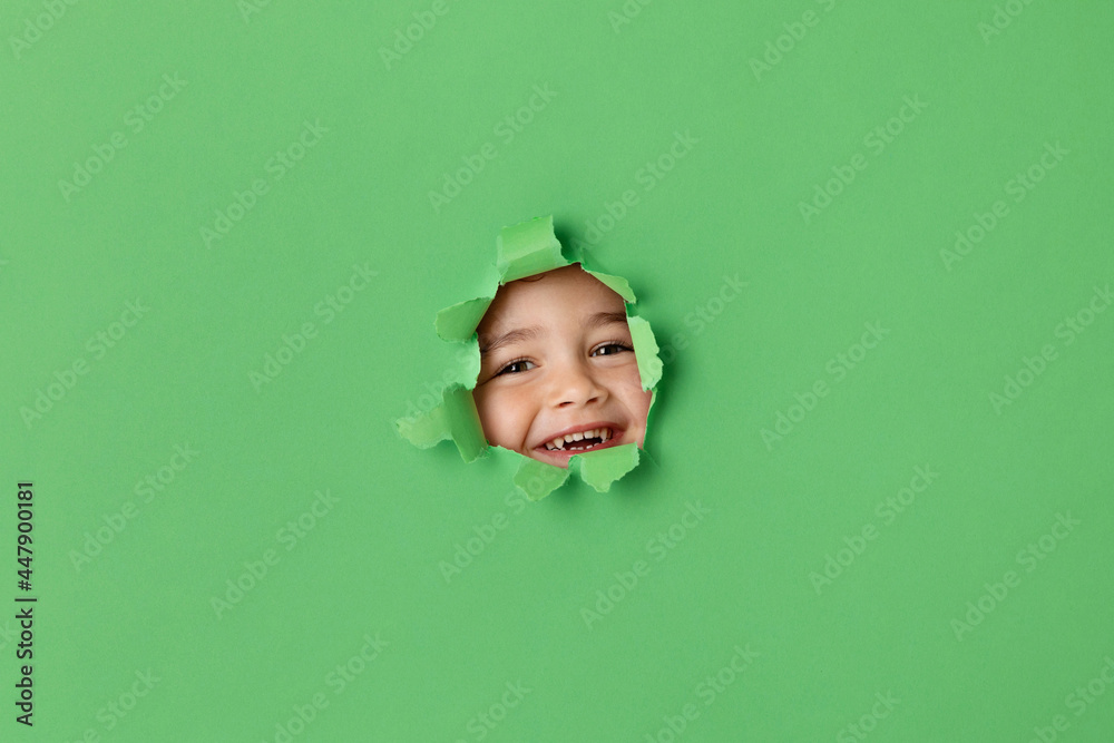 Smiling boy peeking through green torn paper Stock Photo | Adobe Stock