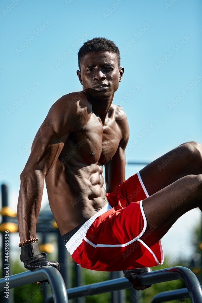 Black young man exercising on the uneven bars in the park, crossfit ...