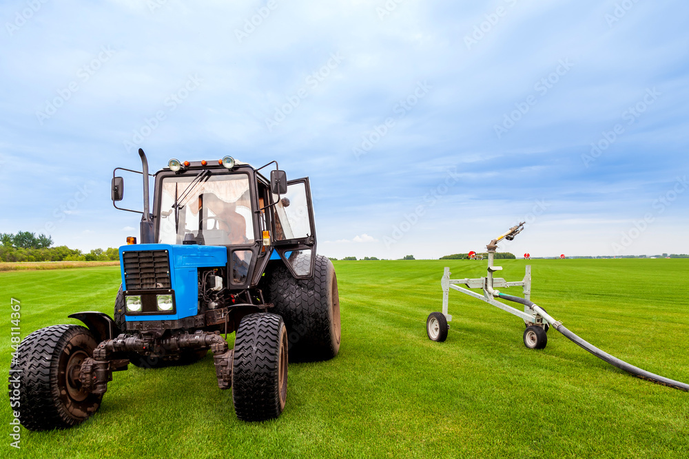 Sprinkler and blue tractor watering agricultural field in the sun ...