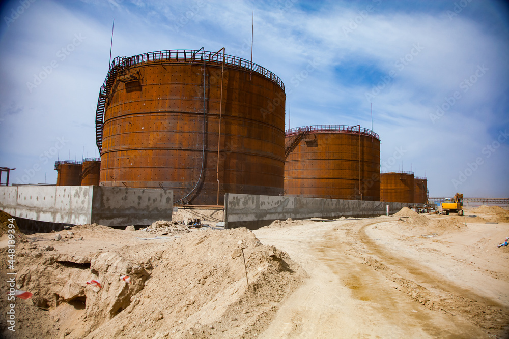 Rusted oil storage tanks on sand and blue sky background. Asphaltic ...