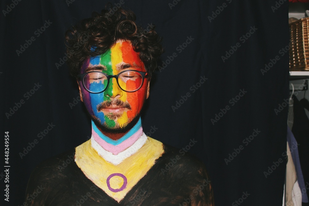 Portrait of young man face painted as lgbtq progress pride flag with ...