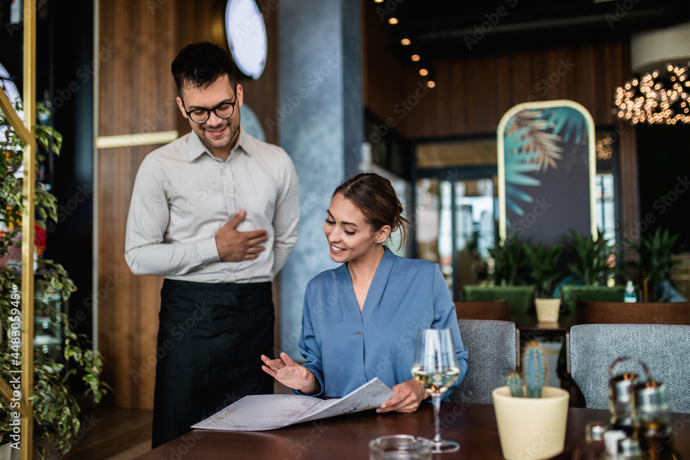Hansome young waiter showing menu to beautiful female customer in ...