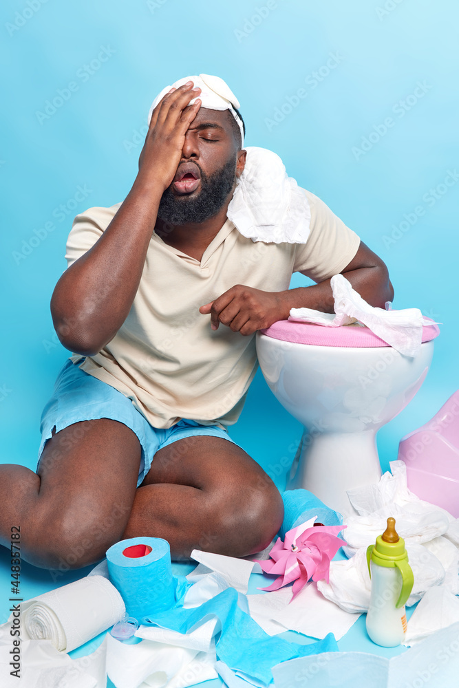 Tired dark skinned man cleans in restroom dressed casually leans on ...