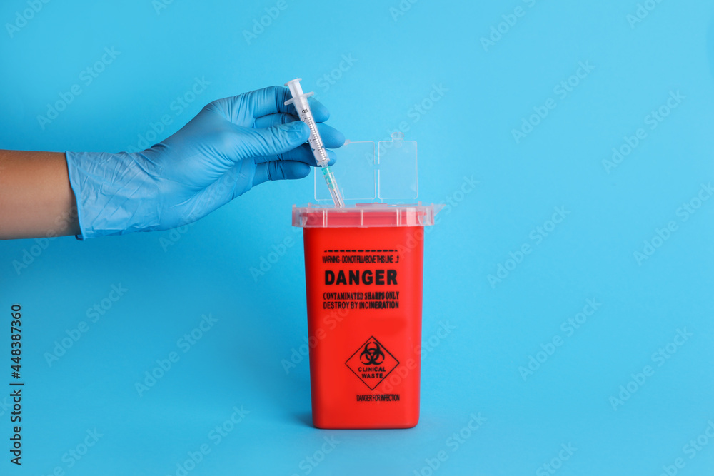 Doctor throwing used syringe into sharps container on light blue ...