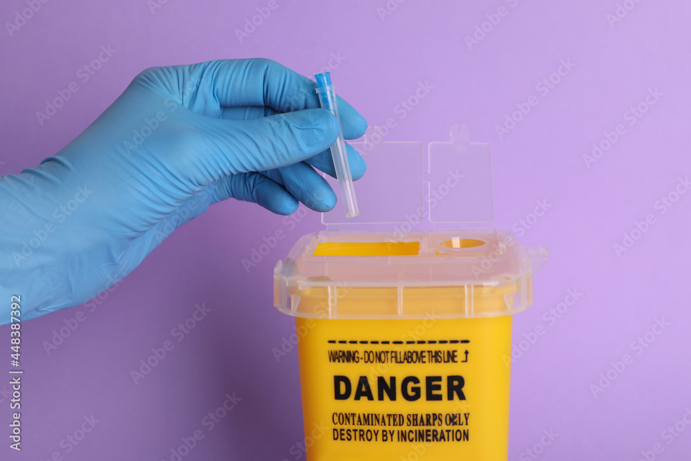 Doctor throwing used syringe needle into sharps container on violet ...