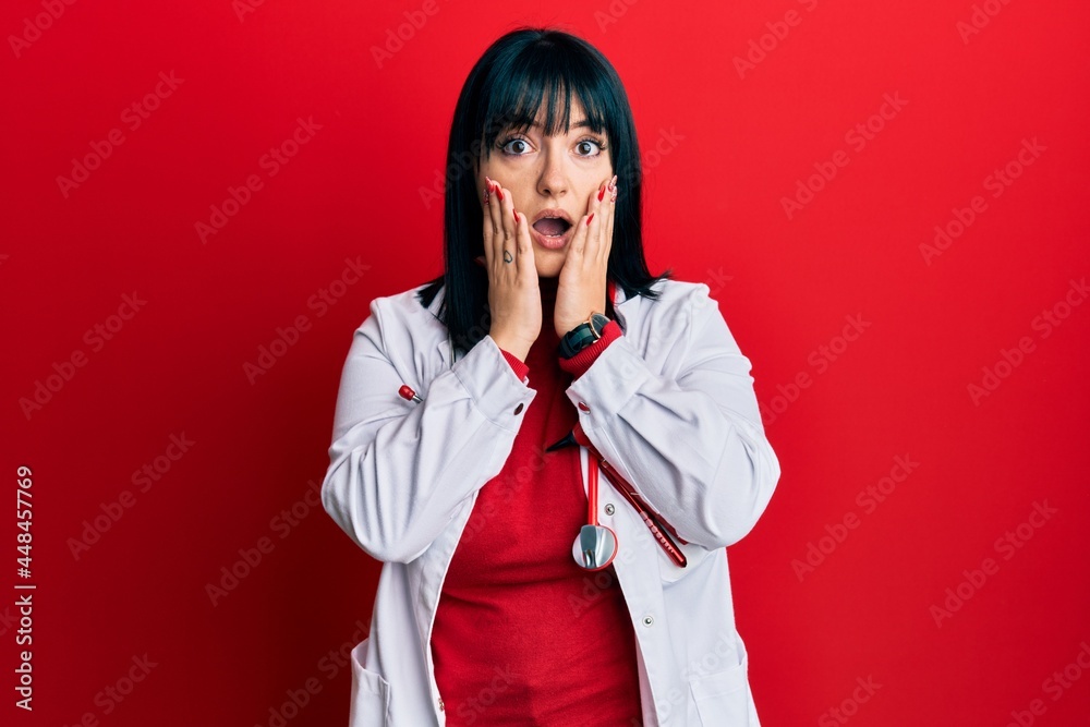 Young hispanic woman wearing doctor uniform and stethoscope afraid and ...