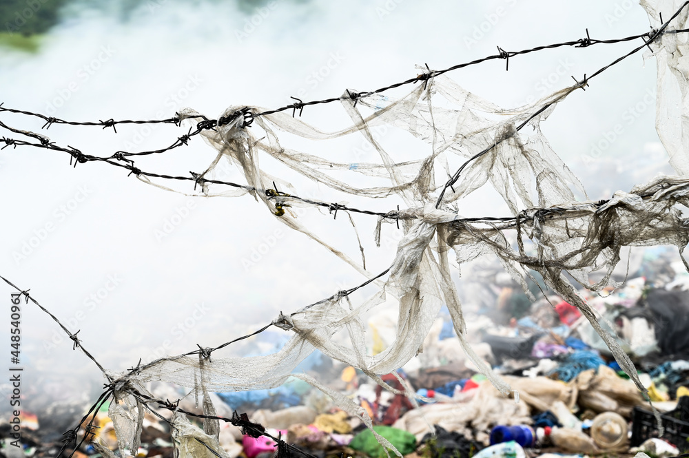 Barbed wire fence around open landfill site with burning waste. Burning ...
