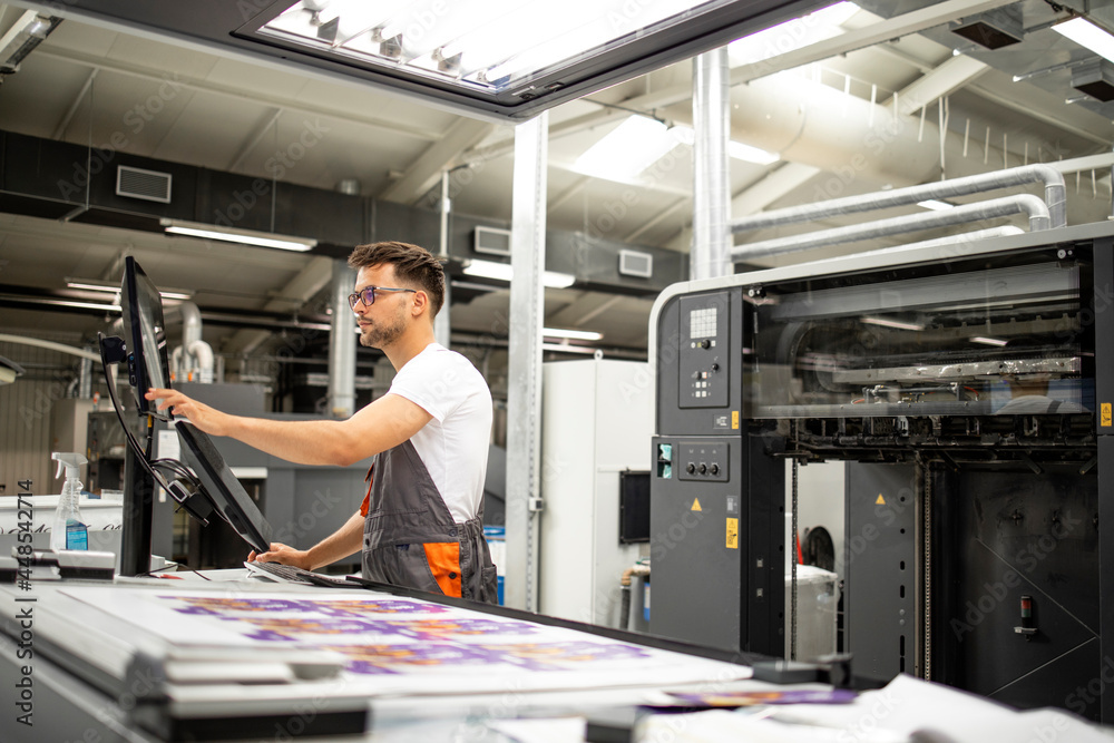 Print house worker setting parameters on modern offset printing machine ...