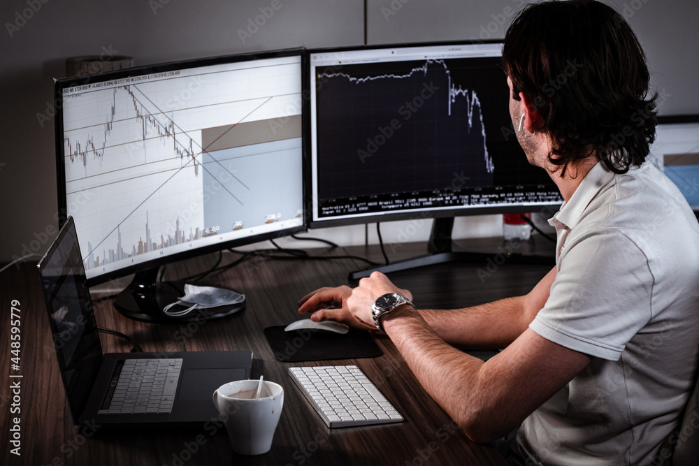 The young trader dressed in a white polo shirt looks at his computer ...