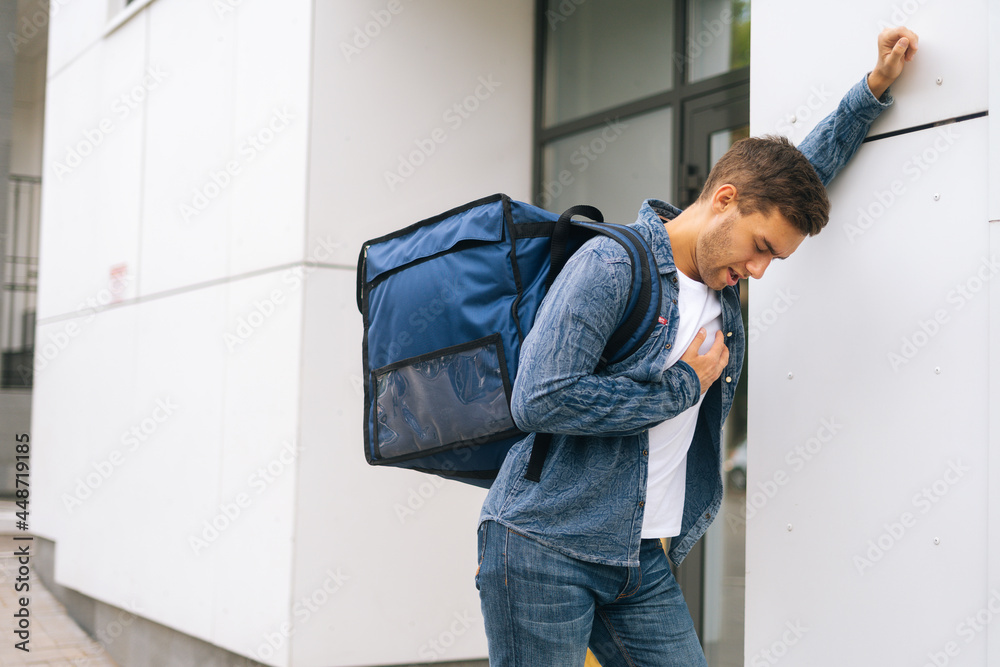 Exhausted food delivery man with large thermo backpack stopping by wall ...